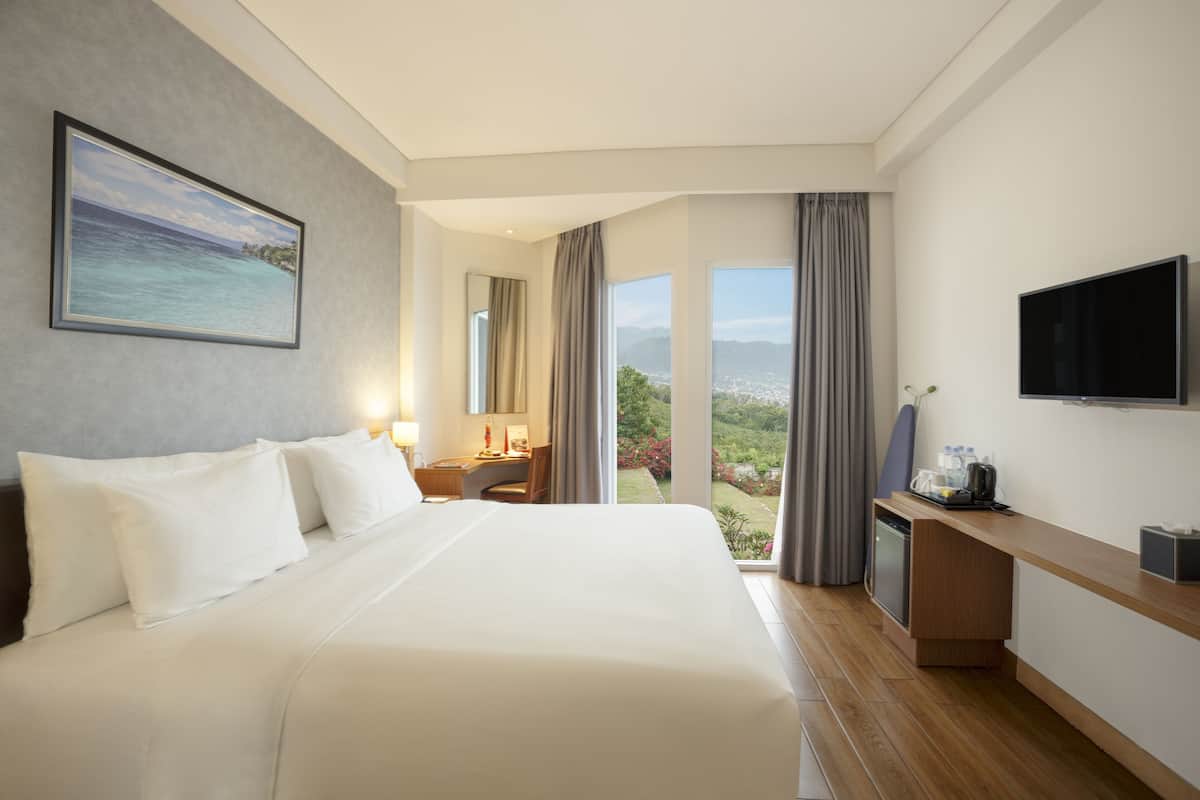 Quarto de hotel com uma cama grande, uma escrivaninha com cadeira, televisão de tela plana e vista para o exterior.