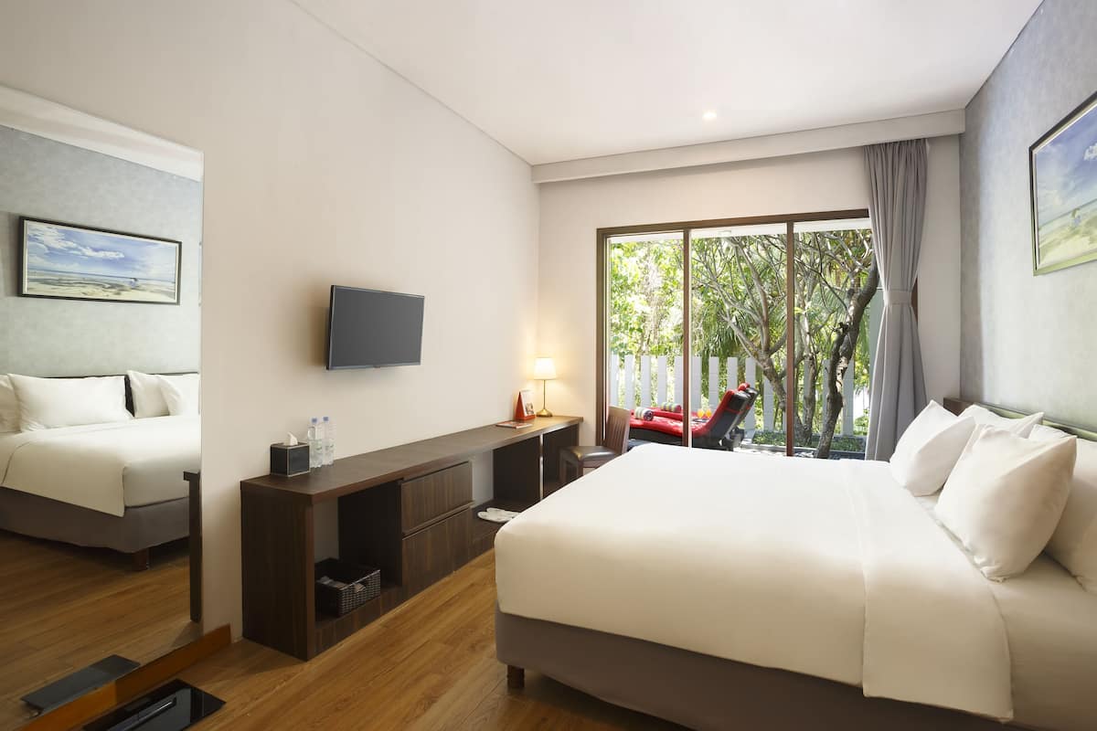 Quarto de hotel com uma cama grande, uma escrivaninha com televisão de tela plana, uma cadeira e janela com vista para árvores.