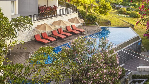 Um hotel moderno com piscina infinita no terraço, cadeiras de lounge vermelhas e uma vista panorâmica do oceano.