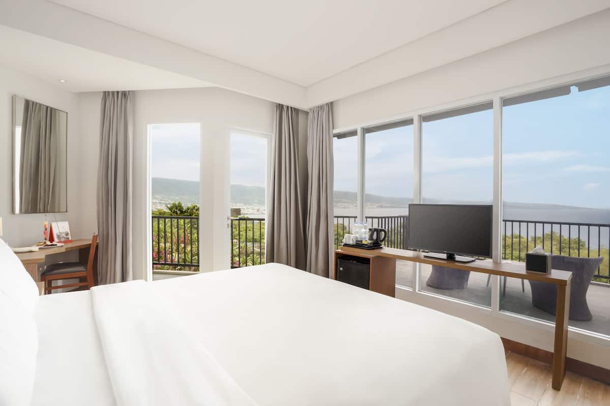 Quarto de hotel com uma cama grande, uma escrivaninha com televisão e varanda com vista para o mar.