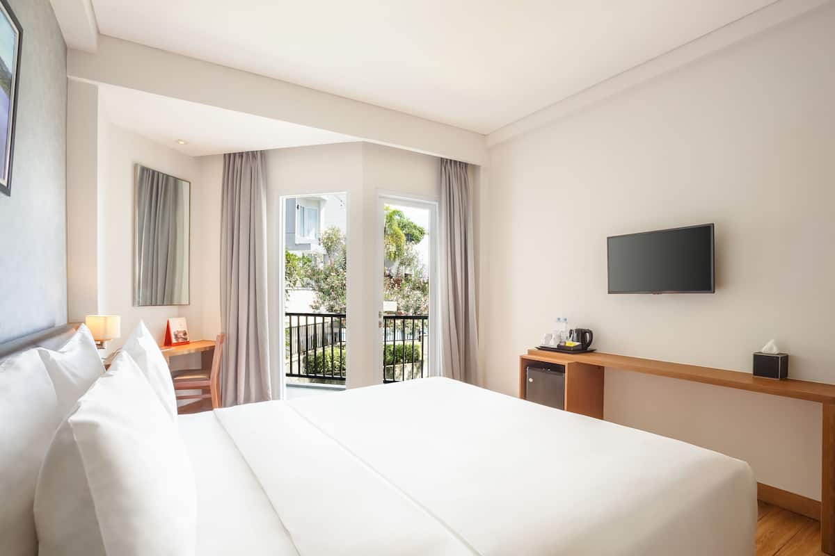 Quarto de hotel com uma cama grande, uma escrivaninha, televisão e varanda com vista para o verde.