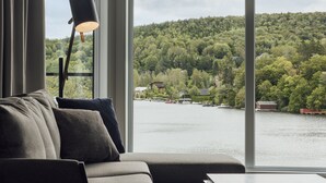 Quarto com uma grande janela que oferece vista para um lago e colinas arborizadas.