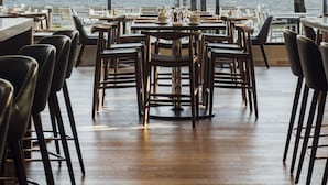 Restaurante com vista para um lago e colinas, com lustre moderno, mesas e cadeiras de madeira.
