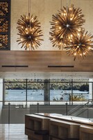 Um interior moderno com duas grandes luminárias pendentes em formato de estrela, uma janela ampla com vista para um lago e uma floresta, e um balcão de recepção de madeira.