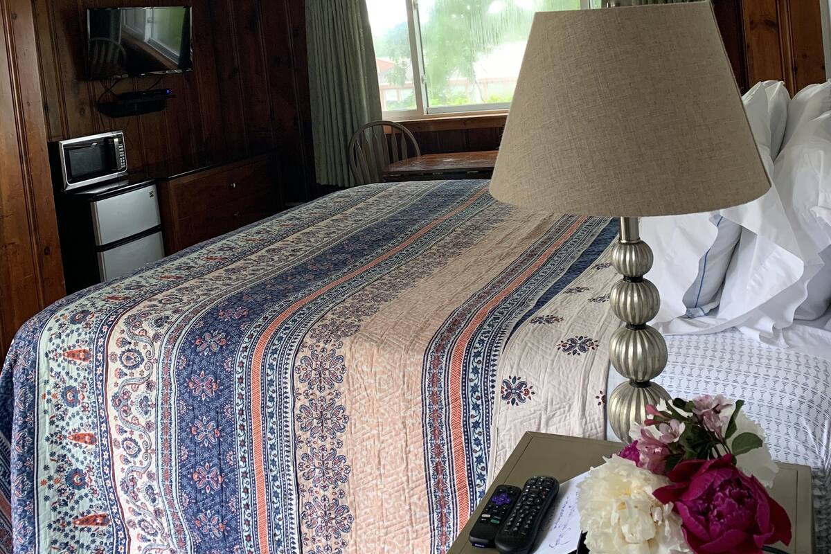 Quarto de hotel com cama, escrivaninha com luminária, televisão, micro-ondas e janela com cortinas.