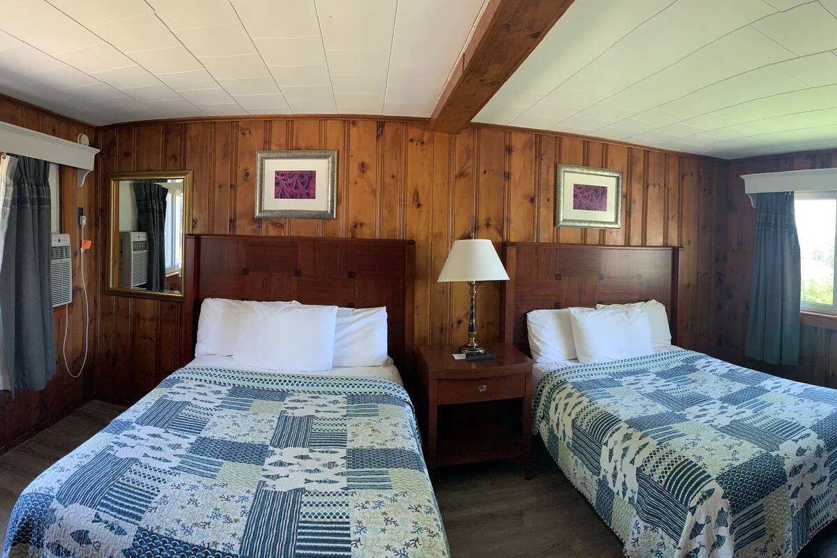 Quarto com duas camas, paredes de painel de madeira e quadros emoldurados.