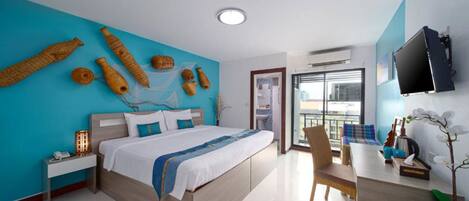 Quarto moderno com uma cama grande, uma escrivaninha e uma cadeira. Há uma TV montada na parede e uma janela com vista para o exterior.