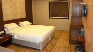 Quarto com cama, mesas de cabeceira, piso de madeira, janela e aquecedor fixado na parede.
