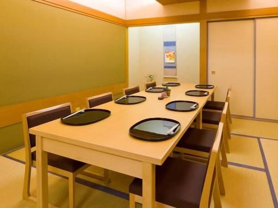 Uma sala de conferências com uma mesa comprida e cadeiras, uma luminária no teto e uma porta ao fundo.