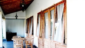 Quarto com teto de madeira, mesa de jantar com cadeiras e grandes janelas com cortinas.
