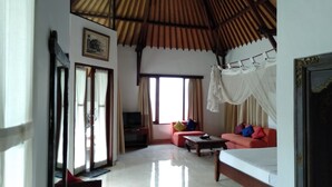 Um quarto espaçoso com teto alto, uma cama, um sofá, uma mesa de centro e uma televisão.
