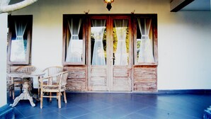 Uma porta de madeira com cortinas, um lustre pendurado e uma mesa redonda com cadeiras em frente a um edifício.