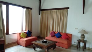 Sala de estar com dois sofás, uma mesa de centro, um abajur e janelas amplas com cortinas.
