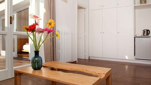 Um quarto com uma mesa de madeira, um vaso com flores, um armário branco e um radiador.