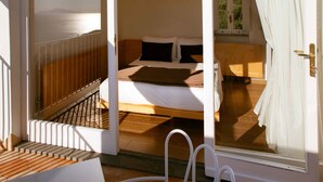 Quarto com cama, travesseiros e cabeceira de madeira. Há uma janela com cortinas e vista para o exterior.