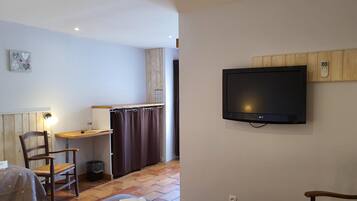 Quarto de hotel com cama, cadeira, escrivaninha, televisão na parede e uma mesinha.
