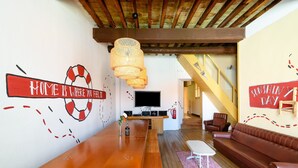 Uma sala de estar espaçosa com piso de madeira, uma grande mesa de madeira, um sofá de couro marrom, uma televisão e uma escada que leva a outro nível.