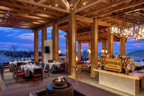 Uma área de refeições ao ar livre com mesas e cadeiras, um bar com uma placa indicando 'QUIVIRA GOLF CLUB', e uma lareira.