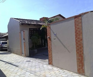 Um imóvel residencial com entrada por calçada pavimentada, portão e pequena área coberta com telhado de azulejos.