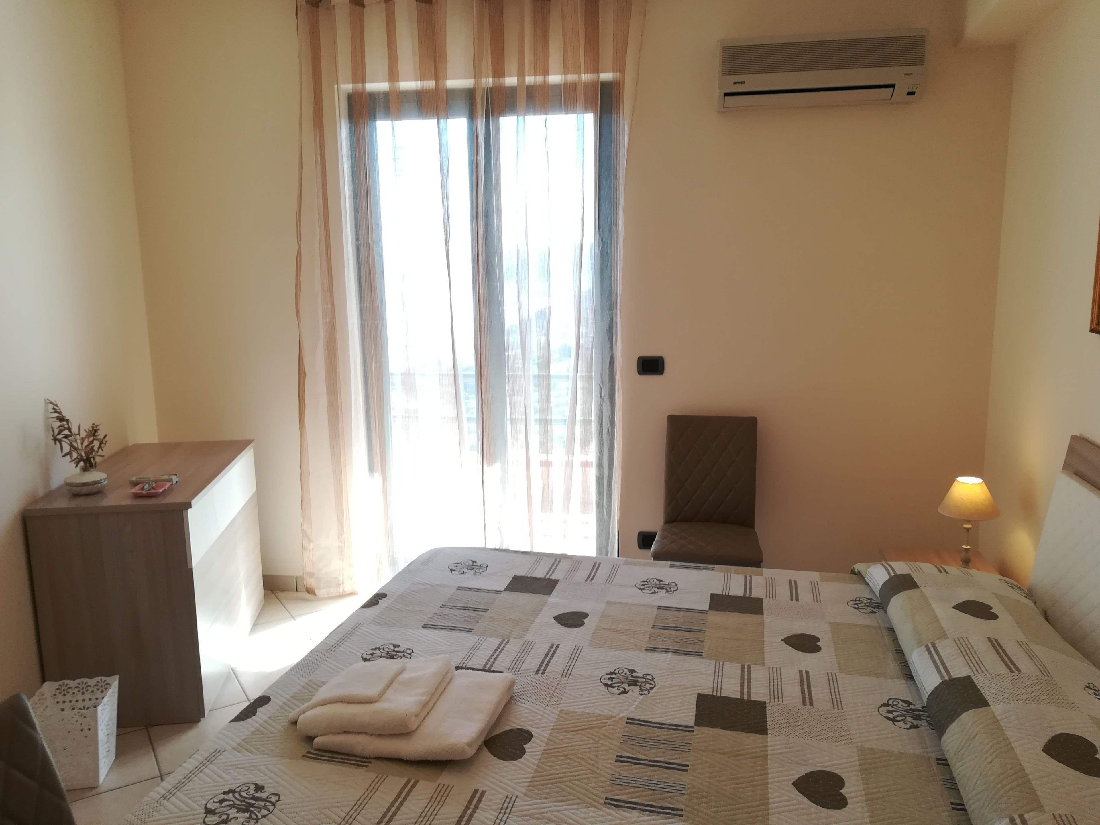 Um quarto com cama, escrivaninha, cadeira e janela com cortinas.