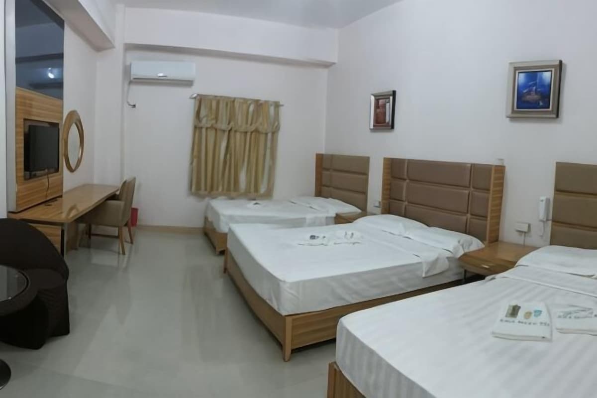 Quarto de hotel com três camas, uma escrivaninha, uma cadeira, aparelho de ar condicionado e uma televisão.