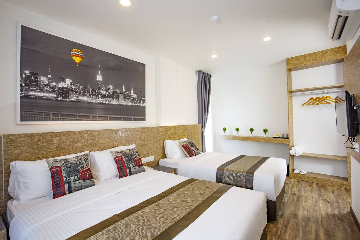 Quarto de hotel com duas camas, uma pintura da paisagem urbana, TV presa à parede e piso de madeira.