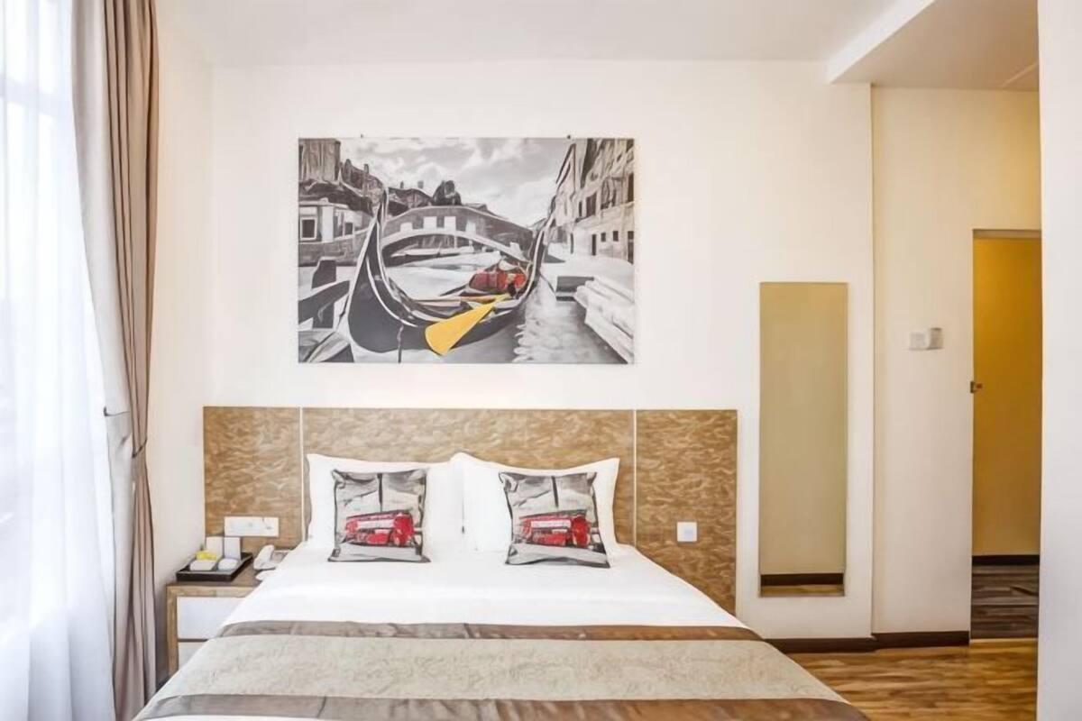 Quarto de hotel com uma cama, um quadro pendurado na parede retratando uma gôndola e uma mesa de cabeceira com abajur.