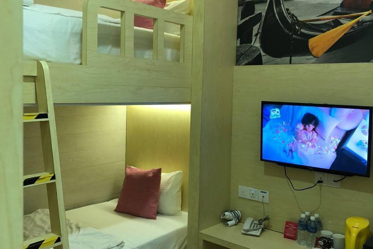 Quarto com beliche, televisão na parede, prateleira pequena com artigos de higiene pessoal e um mural de uma gôndola.
