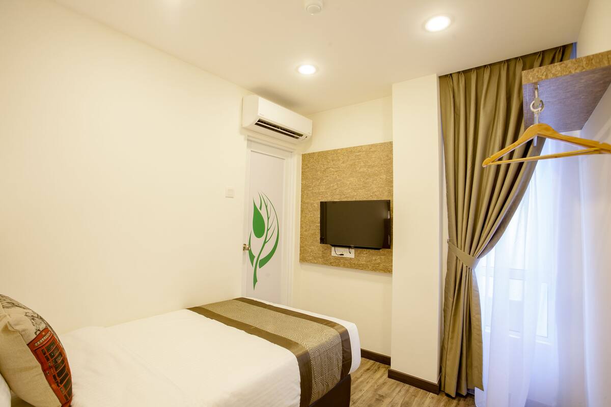Quarto de hotel com cama, televisão fixada na parede, ar condicionado e janela com cortinas.