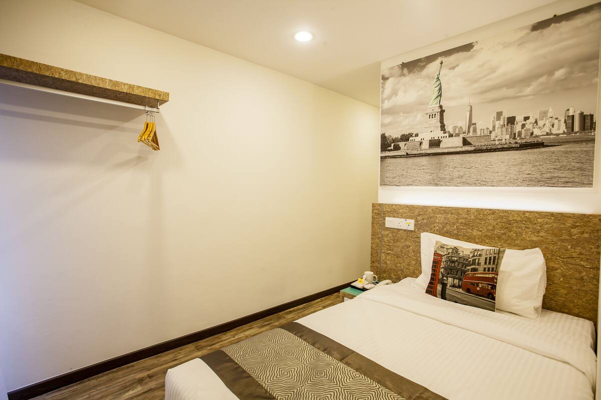 Quarto de hotel com cama, prateleira na parede, pintura da Estátua da Liberdade e tapete estampado.