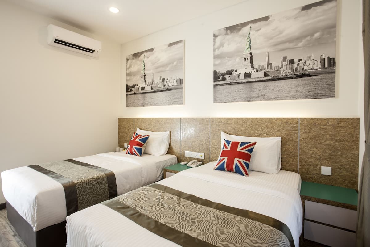 Quarto de hotel com duas camas, uma mesa de cabeceira verde, um telefone e dois aparelhos de ar condicionado fixados na parede.