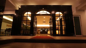 Entrada de hotel com tapete vermelho, portas em arco e vista para o interior.