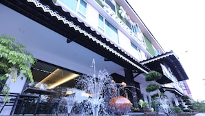 Hotel com uma fonte em frente, passarela coberta e fachada verde e branca.