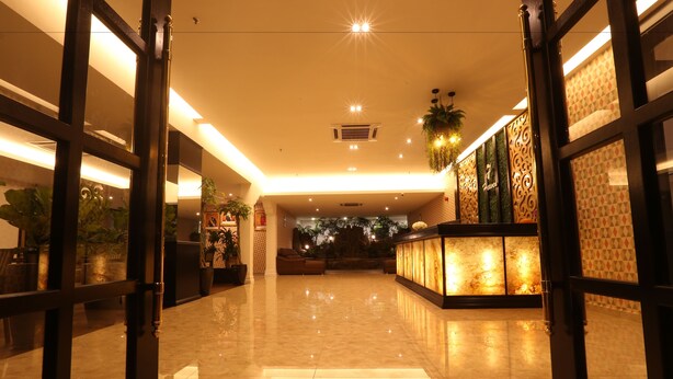 Um hall amplo com piso de mármore, balcão de recepção e plantas em vasos.