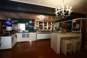 Uma área de bar com balcão, banquetas, um candelabro e uma televisão.