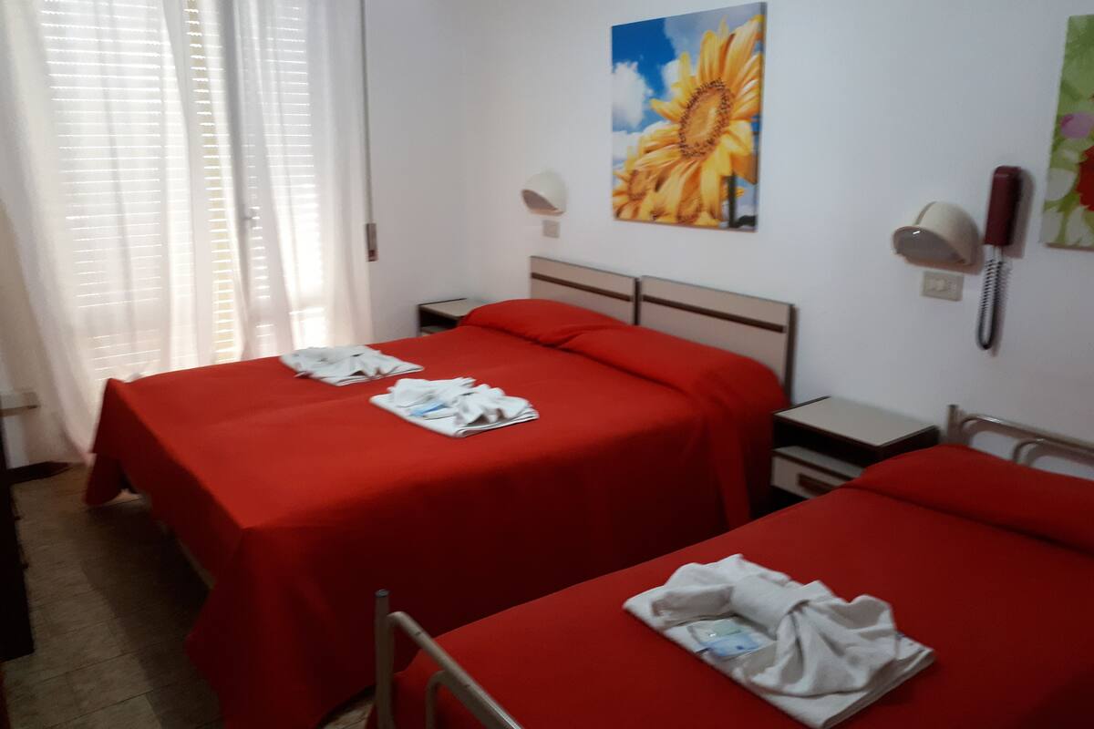 Quarto de hotel com duas camas, um quadro de girassóis na parede, um telefone e uma janela com persianas.