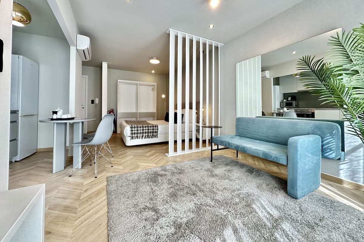Uma sala de estar moderna com um sofá azul, um tapete cinzento e um painel branco.