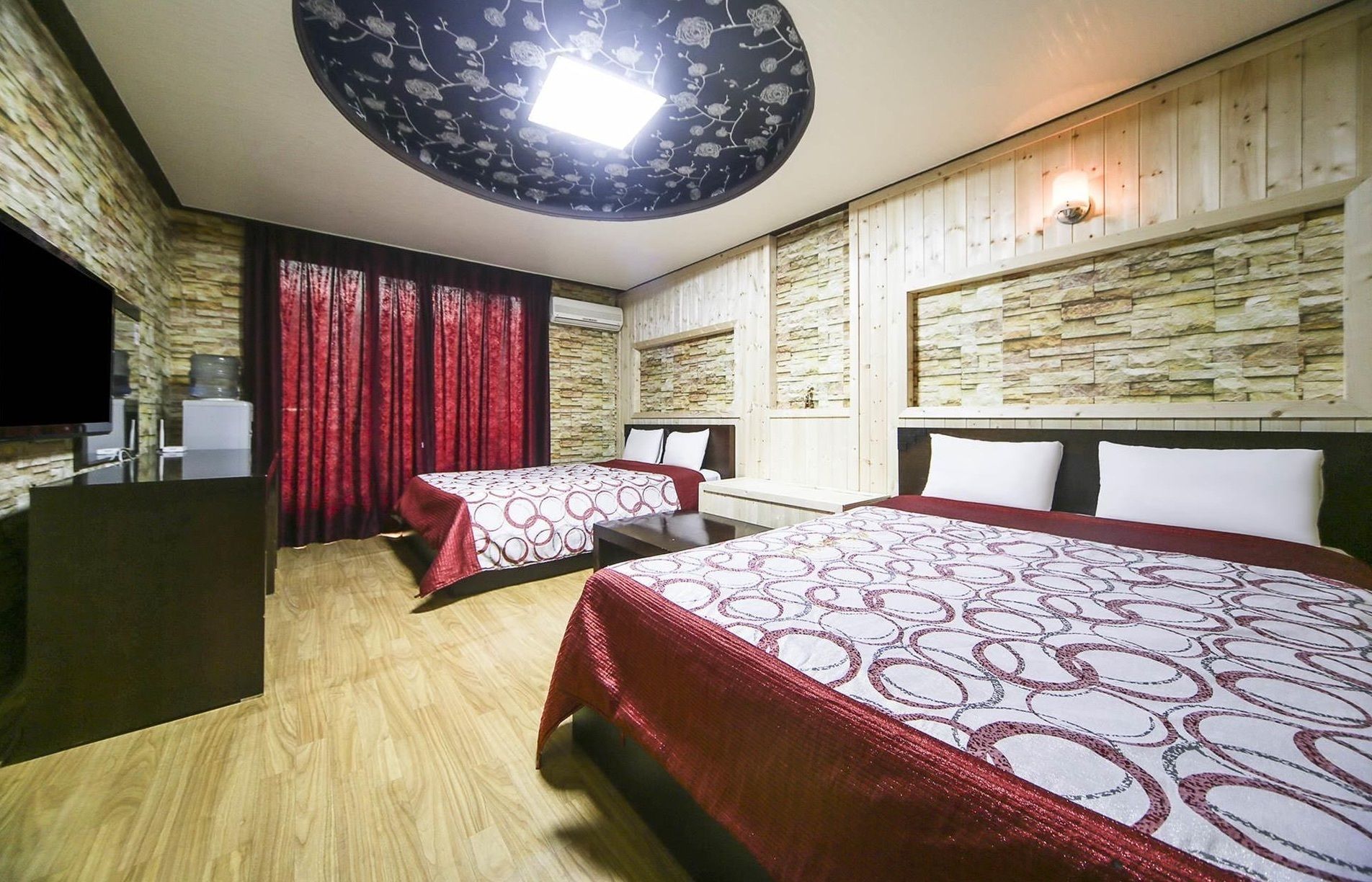 Quarto de hotel com duas camas, um espelho grande, uma televisão e uma parede de pedra.