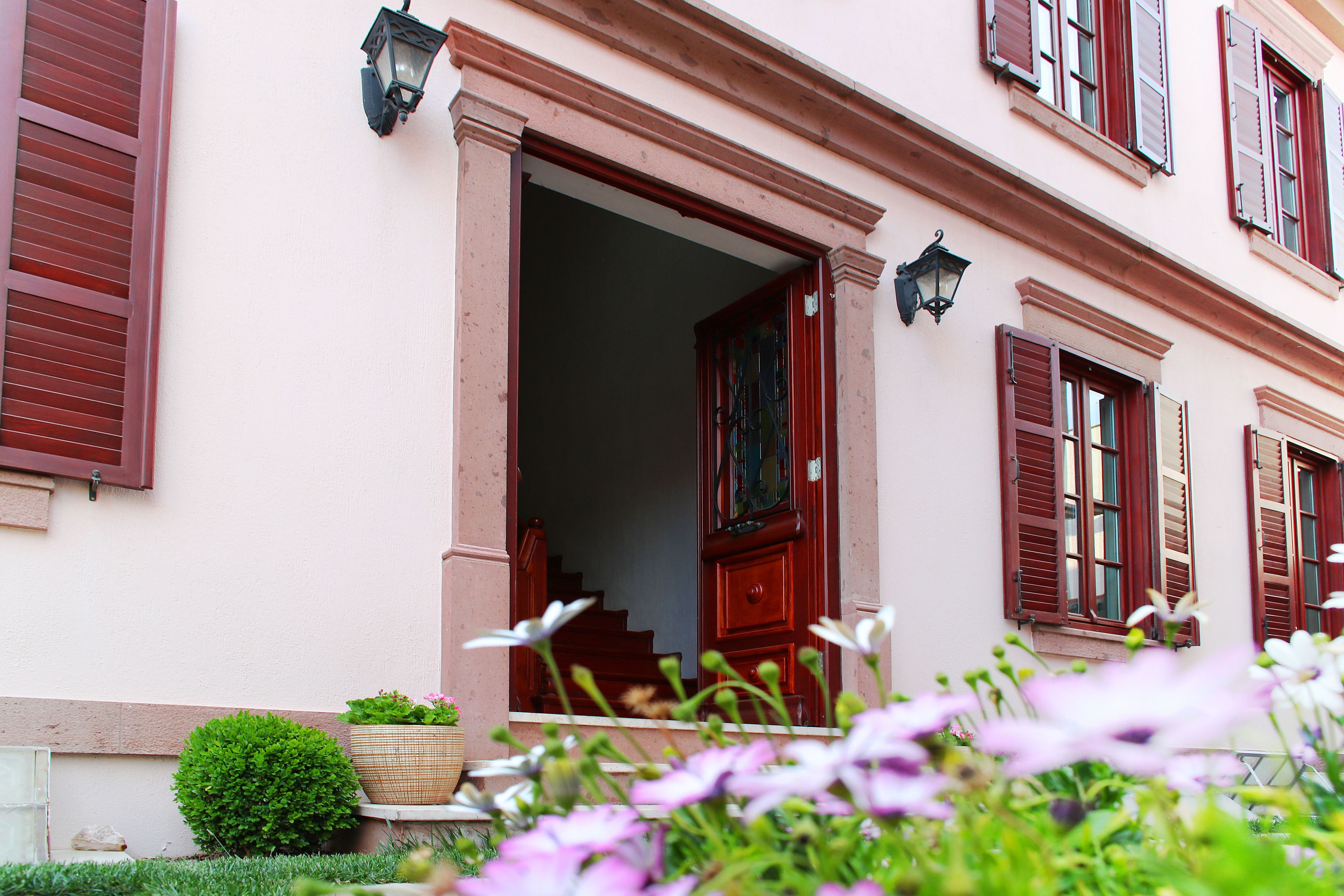 Um edifício com fachada rosa, persianas de madeira e uma escadaria que leva à entrada.
