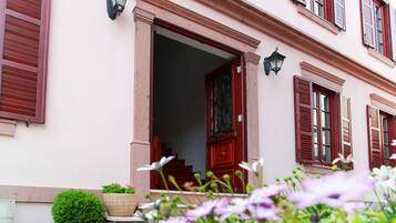 Um edifício com fachada rosa, persianas de madeira e uma escadaria que leva à entrada.