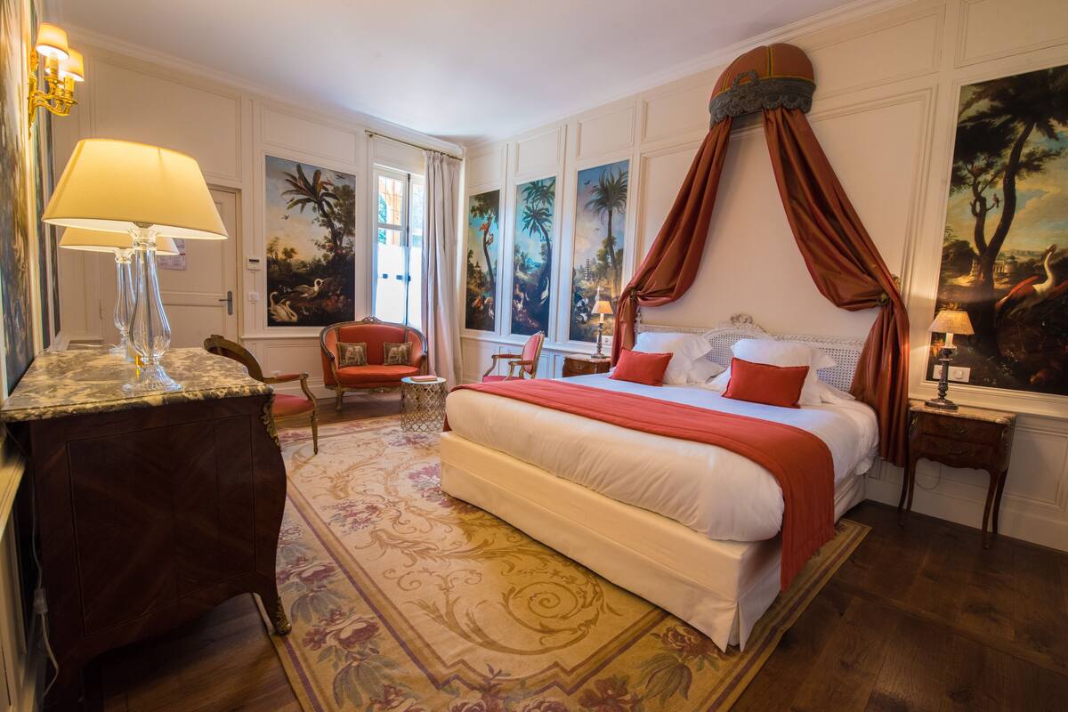 Quarto com cama grande, mesa de cabeceira, cadeira e escrivaninha com abajur.