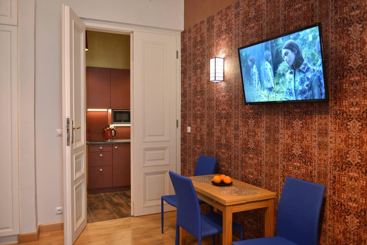 Uma sala de jantar com mesa, cadeiras e uma televisão na parede.