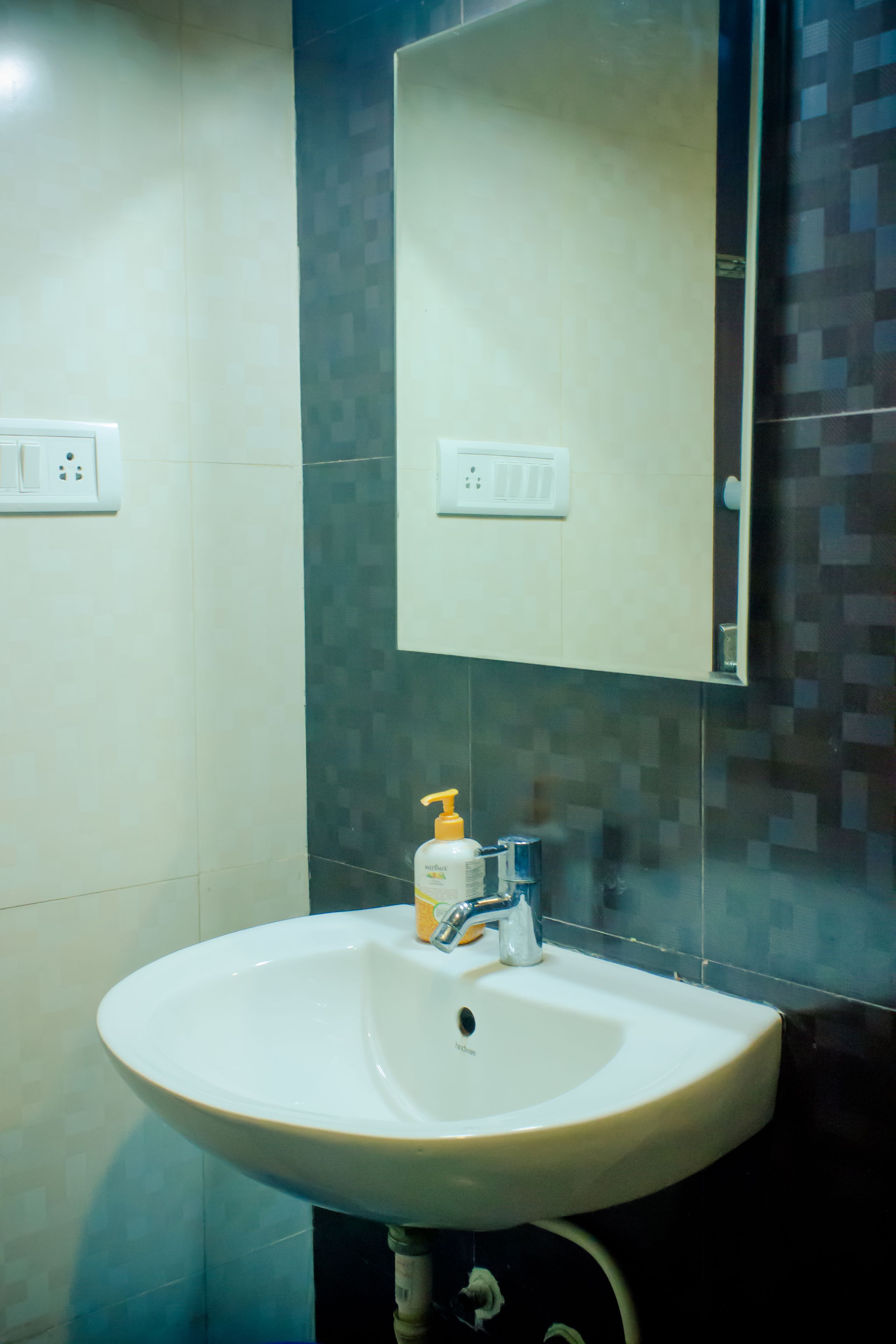 Casa de banho com lavatório branco, espelho e parede revestida a azulejos.