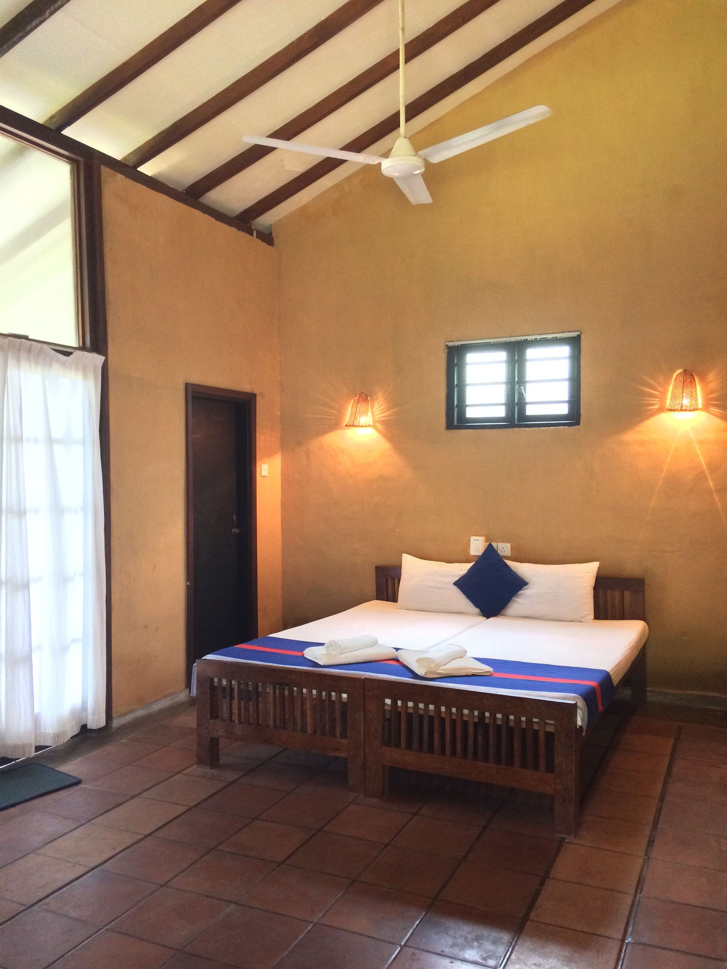 Quarto com cama, ventoinha no teto, janela e luminárias fixadas na parede.