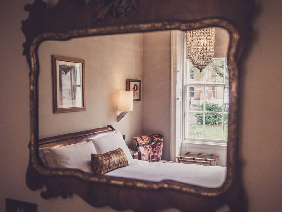 Quarto com um espelho grande refletindo uma cama, uma janela com vista para vegetação e um candelabro.
