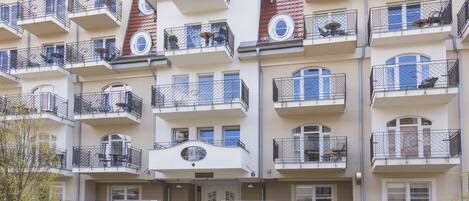Um edifício residencial de vários andares com varandas, uma entrada central e uma escadaria que leva à entrada.
