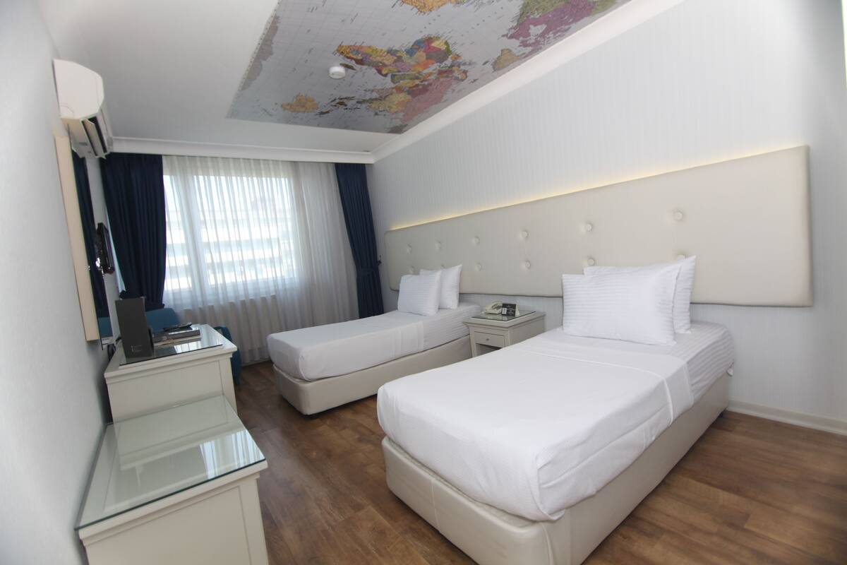 Quarto de hotel com duas camas, uma mesa e um mapa no teto.