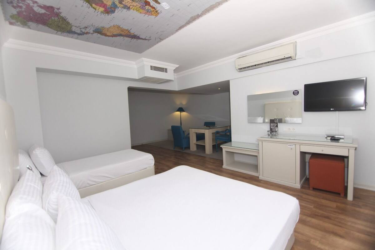 Quarto de hotel com cama, escrivaninha, cadeira, televisão e um mapa no teto.