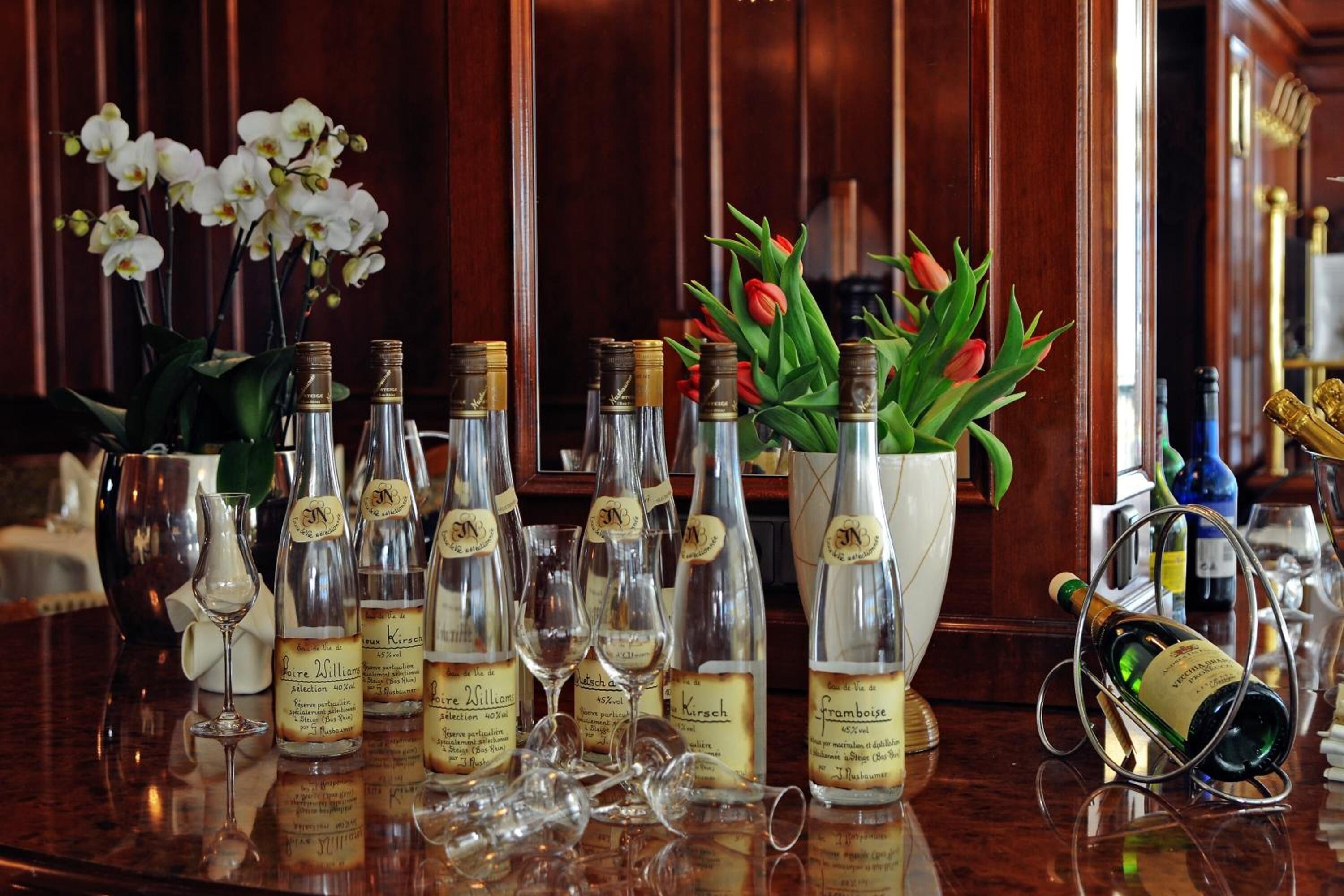 Uma área de bar com várias garrafas de vinho, copos e flores.
