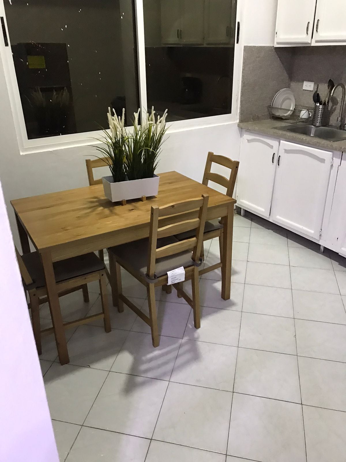 Uma sala de jantar com uma mesa e cadeiras de madeira, uma planta em vaso e armários brancos.